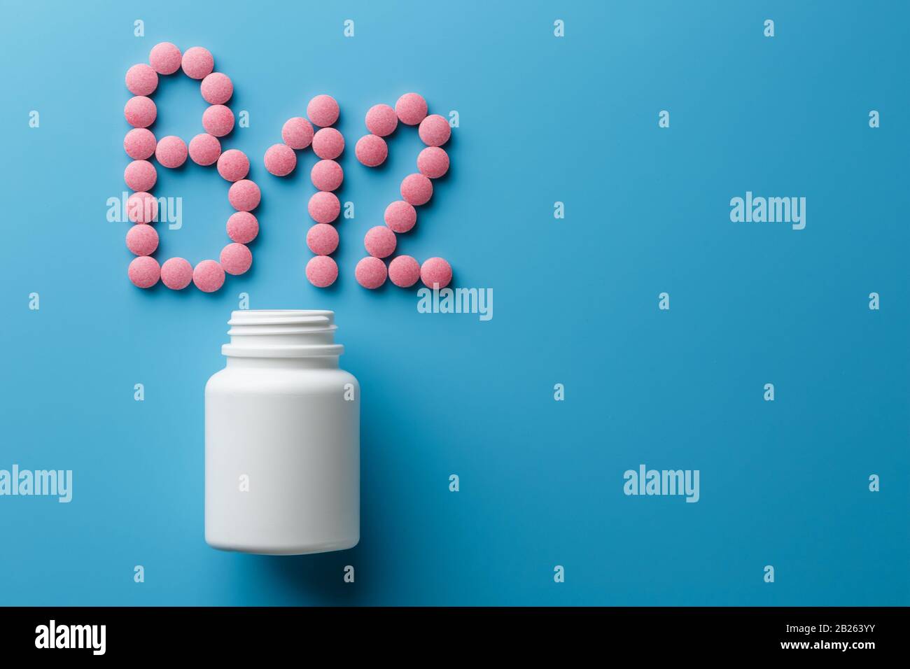 Pink pills in the shape of the letter B12 on a blue background, spilled ...