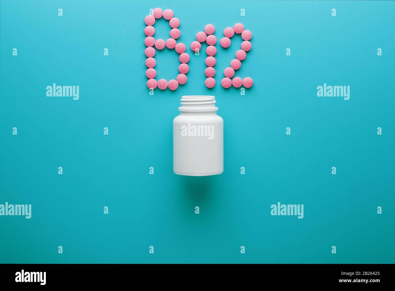 Pink pills in the shape of the letter B12 on a blue background, spilled ...