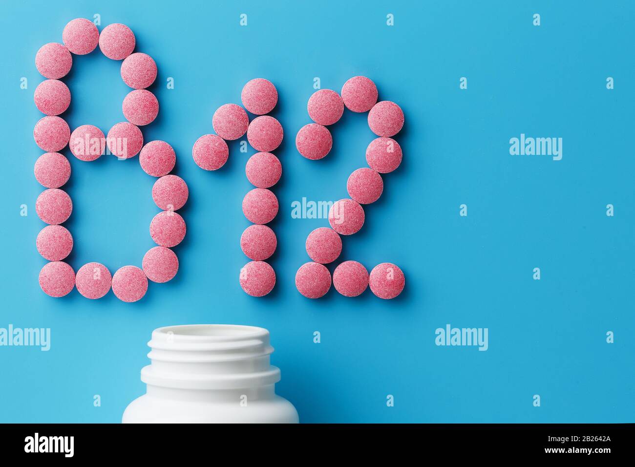Pink pills in the shape of the letter B12 on a blue background, spilled ...