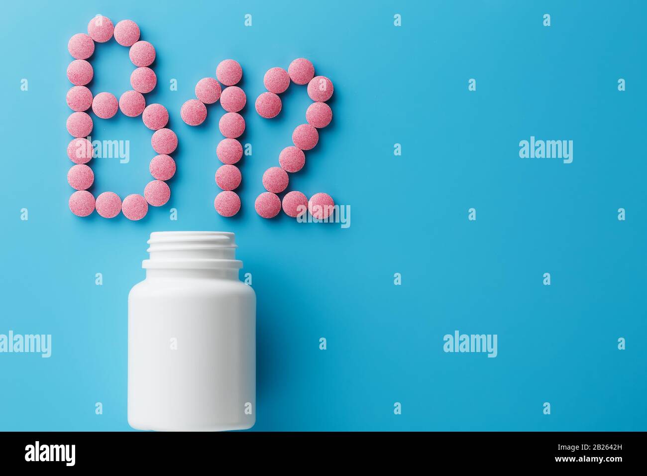 Pink pills in the shape of the letter B12 on a blue background, spilled ...