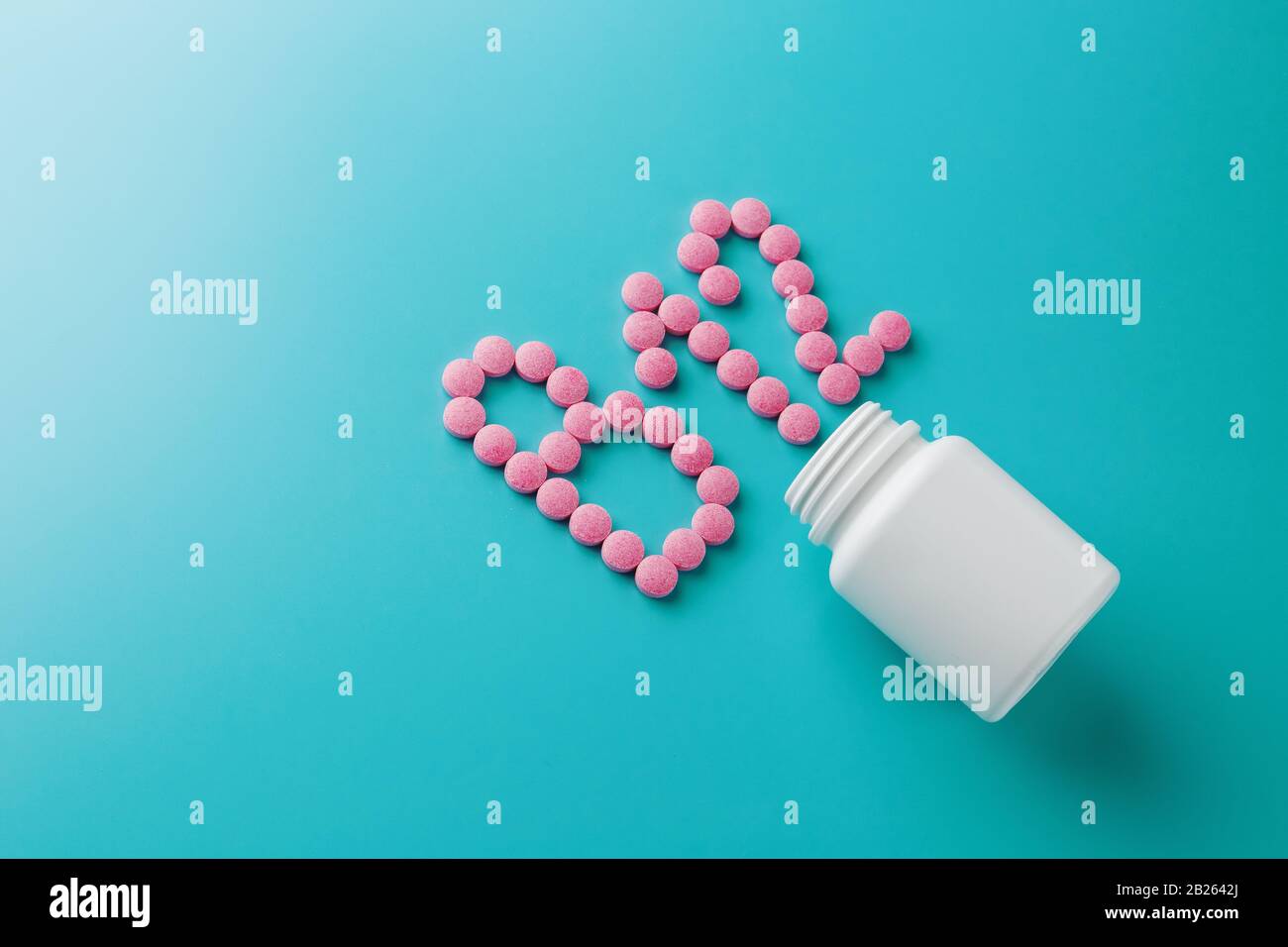 Pink pills in the shape of the letter B12 on a blue background, spilled ...