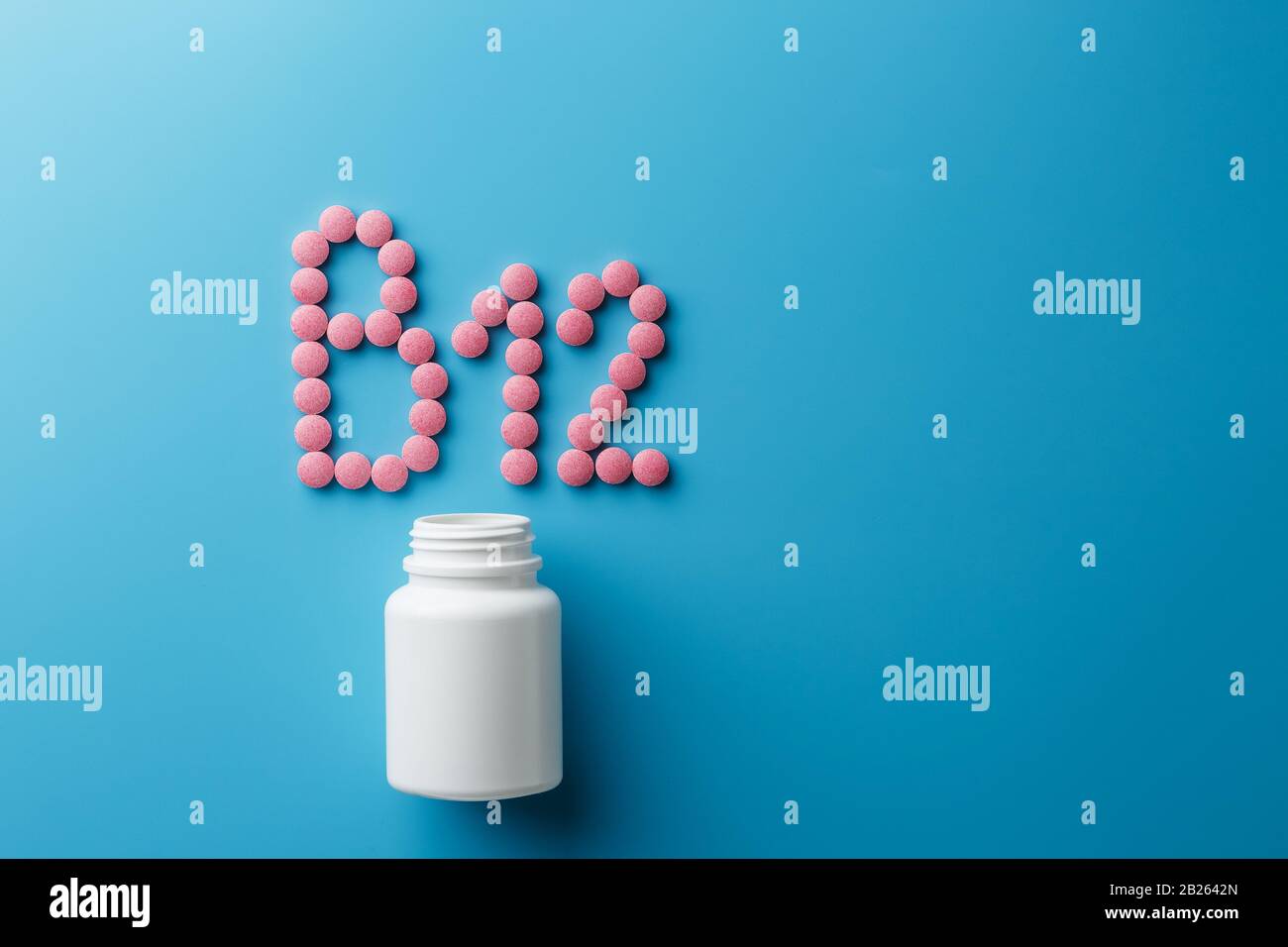 Pink pills in the shape of the letter B12 on a blue background, spilled ...
