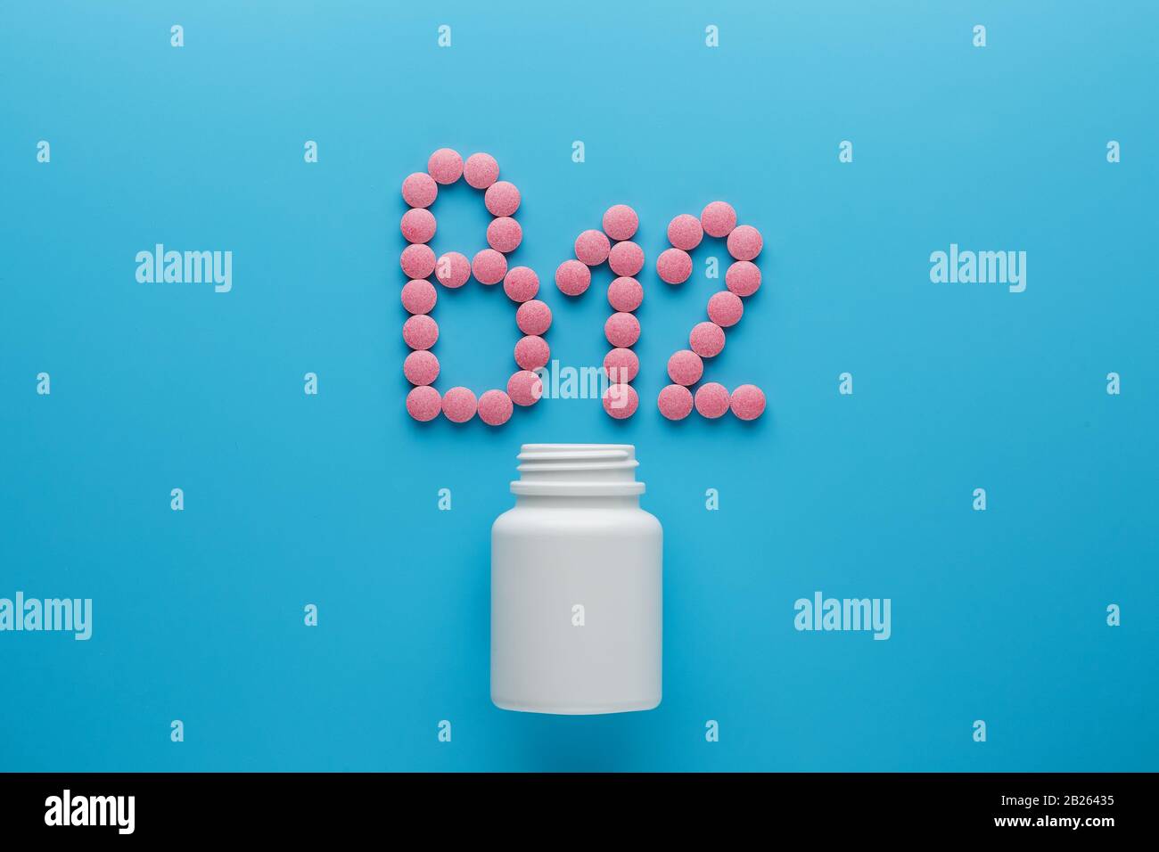 Pink pills in the shape of the letter B12 on a blue background, spilled ...