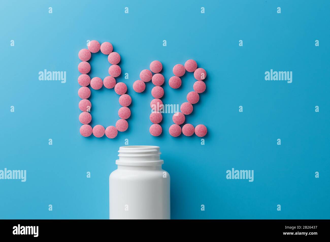 Pink pills in the shape of the letter B12 on a blue background, spilled ...