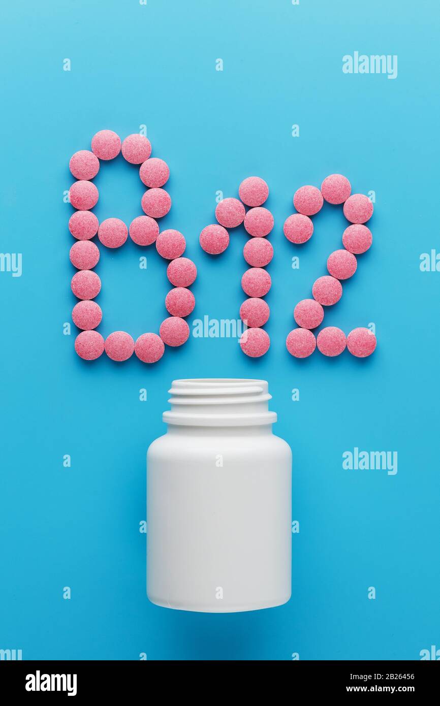 Pink pills in the shape of the letter B12 on a blue background, spilled ...