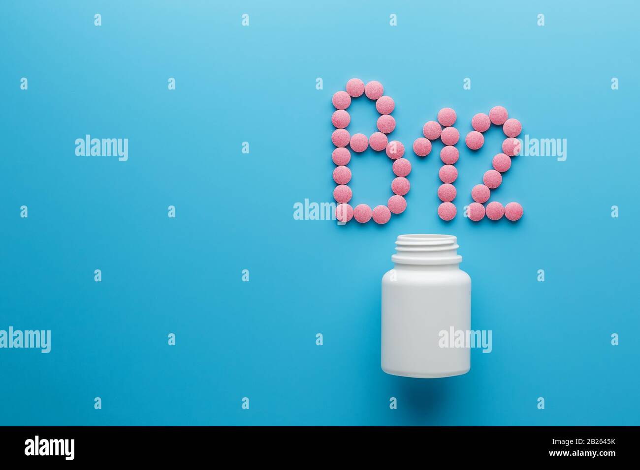 Pink pills in the shape of the letter B12 on a blue background, spilled ...