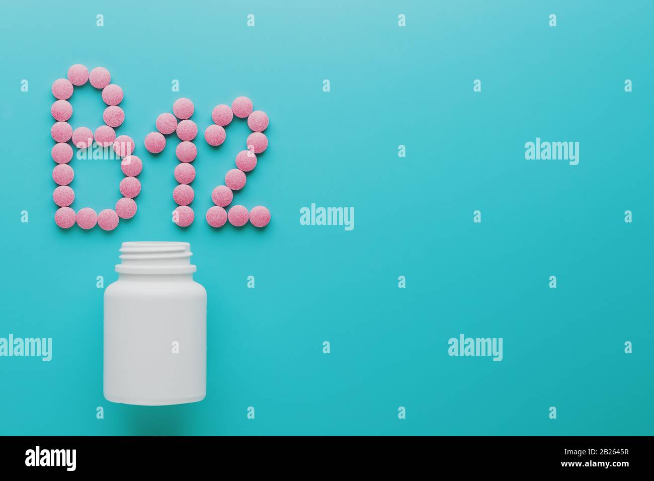Pink pills in the shape of the letter B12 on a blue background, spilled ...
