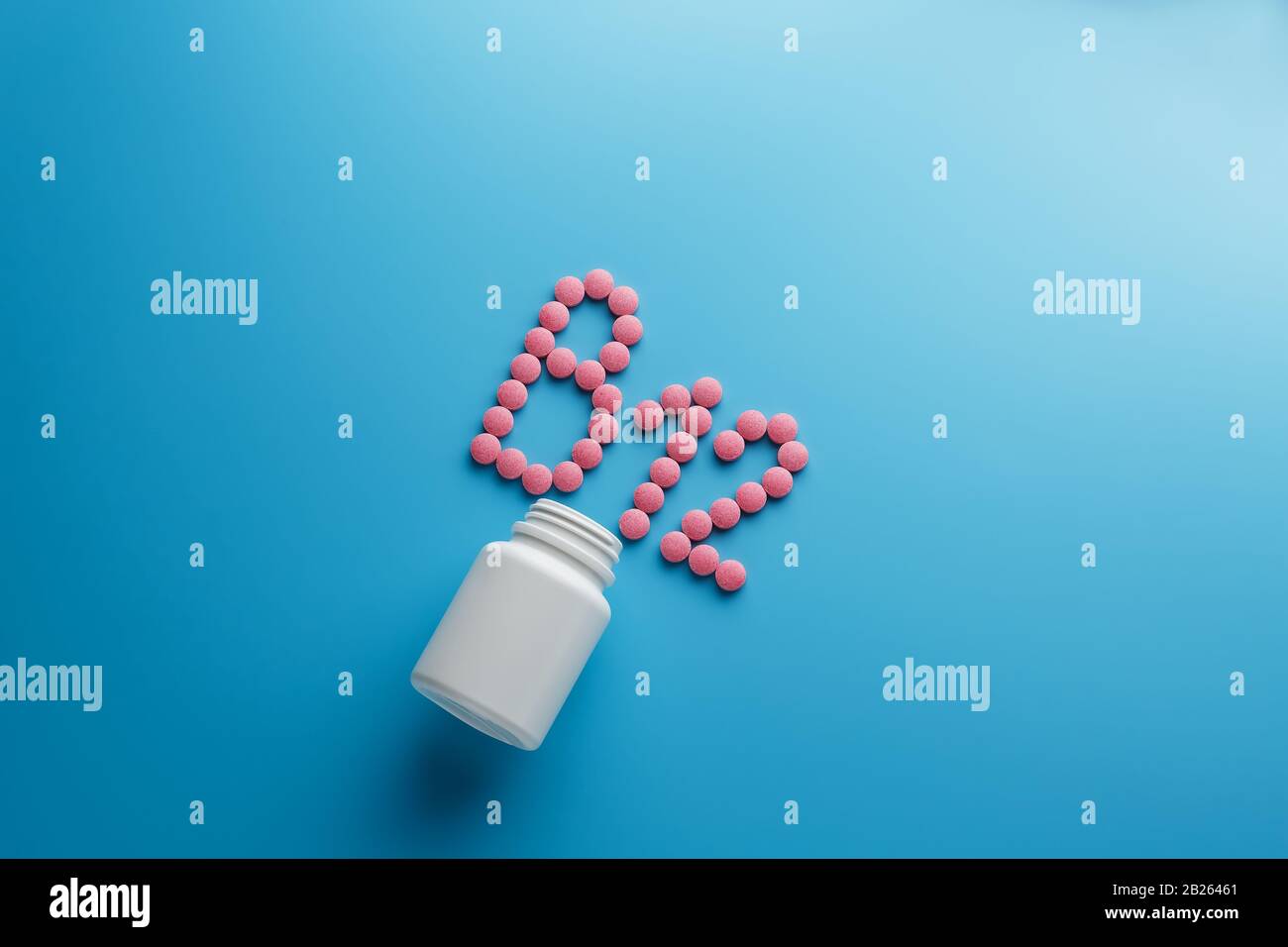 Pink pills in the shape of the letter B12 on a blue background, spilled ...