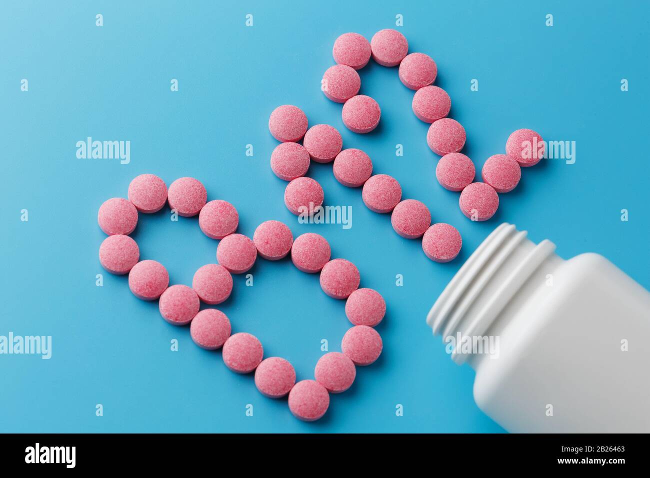 Pink pills in the shape of the letter B12 on a blue background, spilled ...