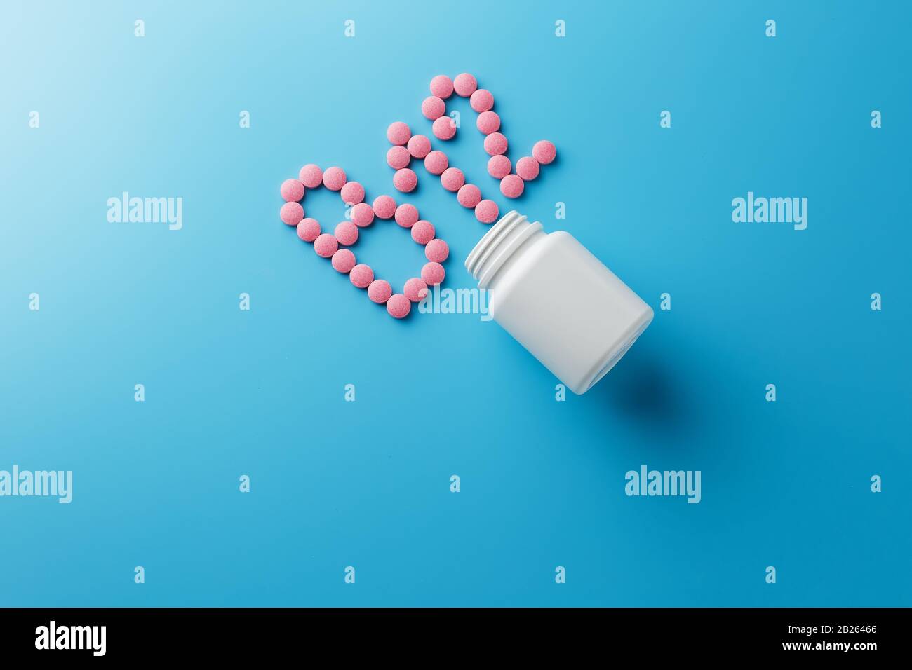 Pink pills in the shape of the letter B12 on a blue background, spilled ...