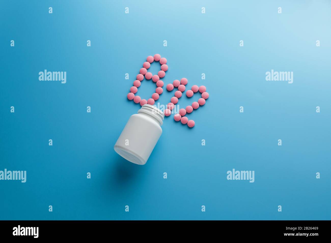 Pink pills in the shape of the letter B12 on a blue background, spilled ...