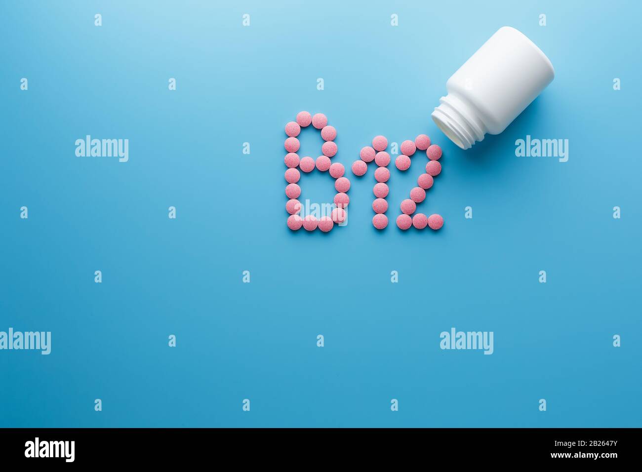Pink pills in the shape of the letter B12 on a blue background, spilled ...