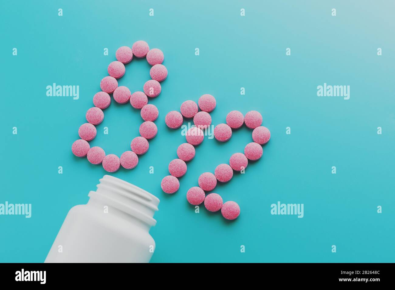 Pink pills in the shape of the letter B12 on a blue background, spilled ...