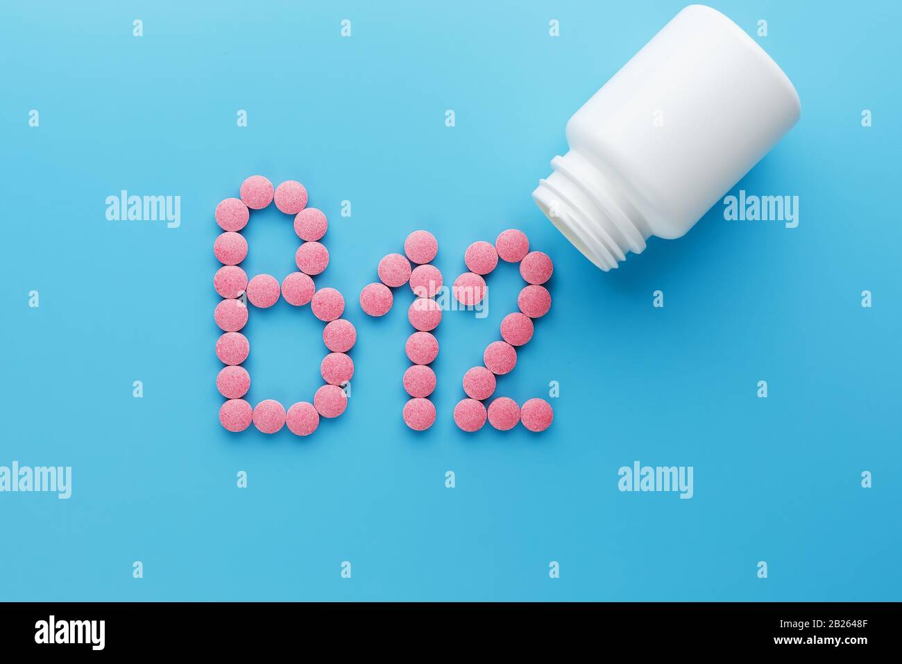 Pink pills in the shape of the letter B12 on a blue background, spilled ...