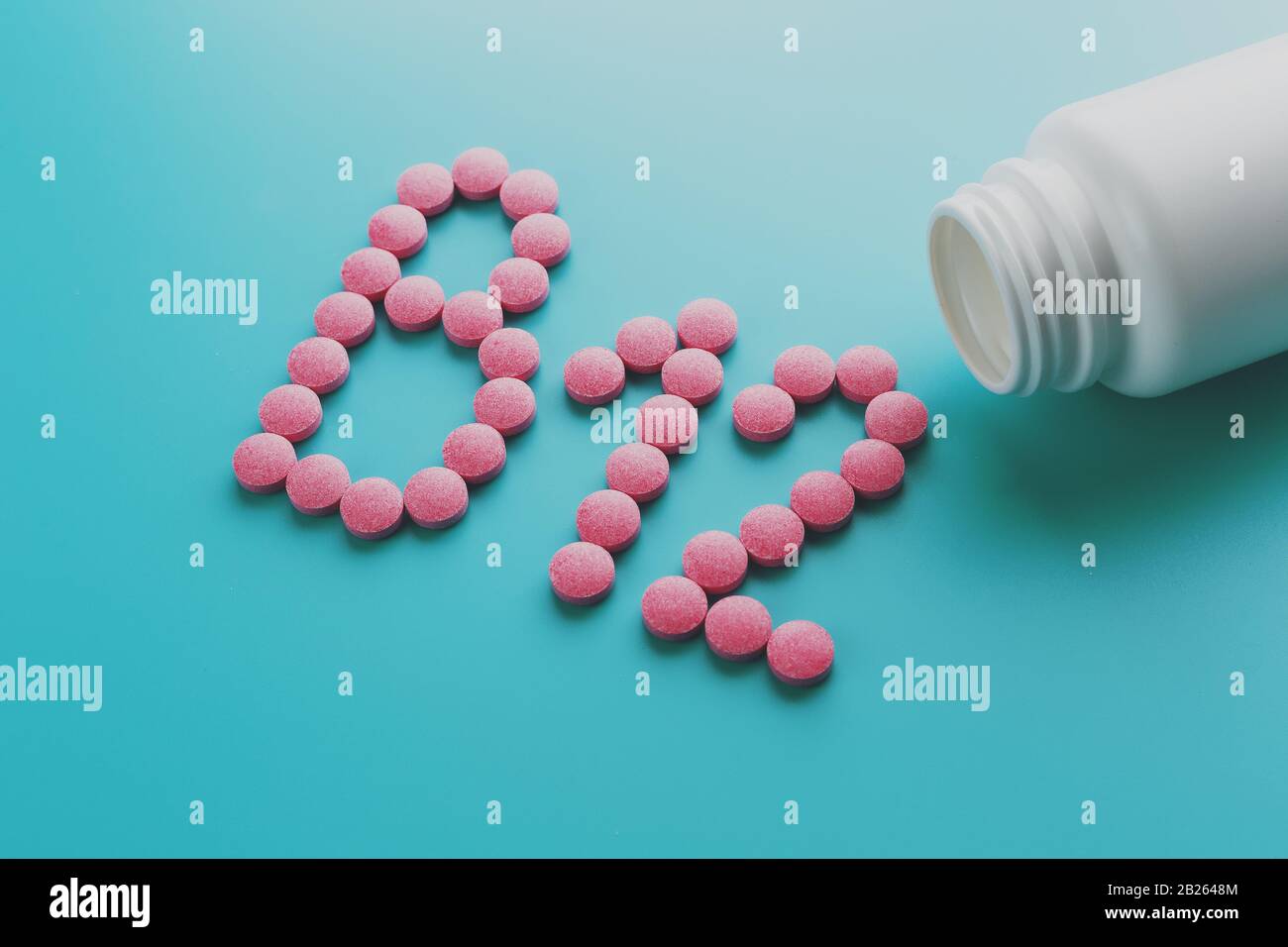 Pink pills in the shape of the letter B12 on a blue background, spilled ...