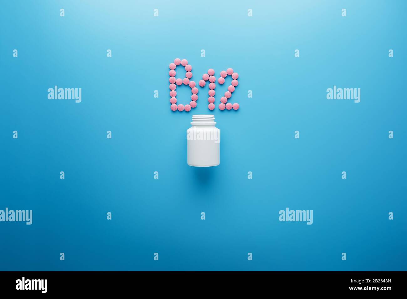 Pink pills in the shape of the letter B12 on a blue background, spilled ...