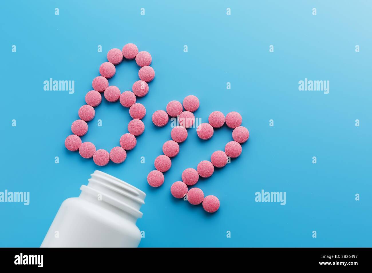 Pink pills in the shape of the letter B12 on a blue background, spilled ...