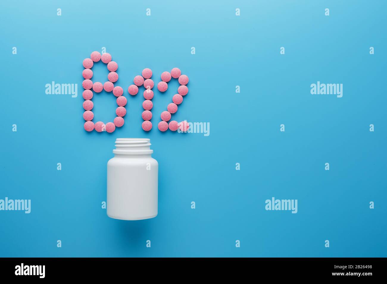Pink pills in the shape of the letter B12 on a blue background, spilled ...