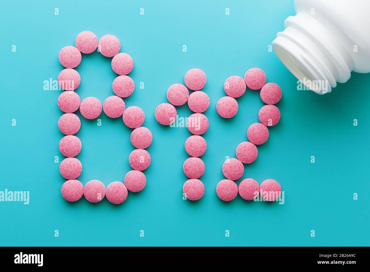 Pink pills in the shape of the letter B12 on a blue background, spilled ...