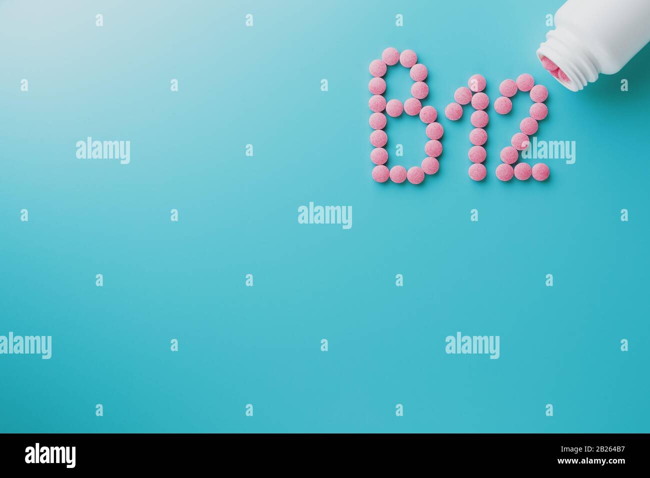 Pink pills in the shape of the letter B12 on a blue background, spilled ...