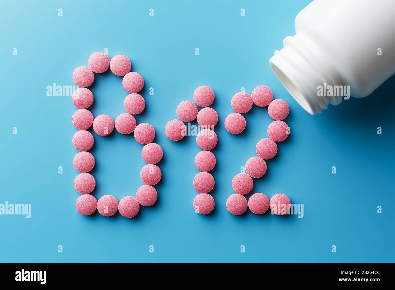 Pink pills in the shape of the letter B12 on a blue background, spilled ...