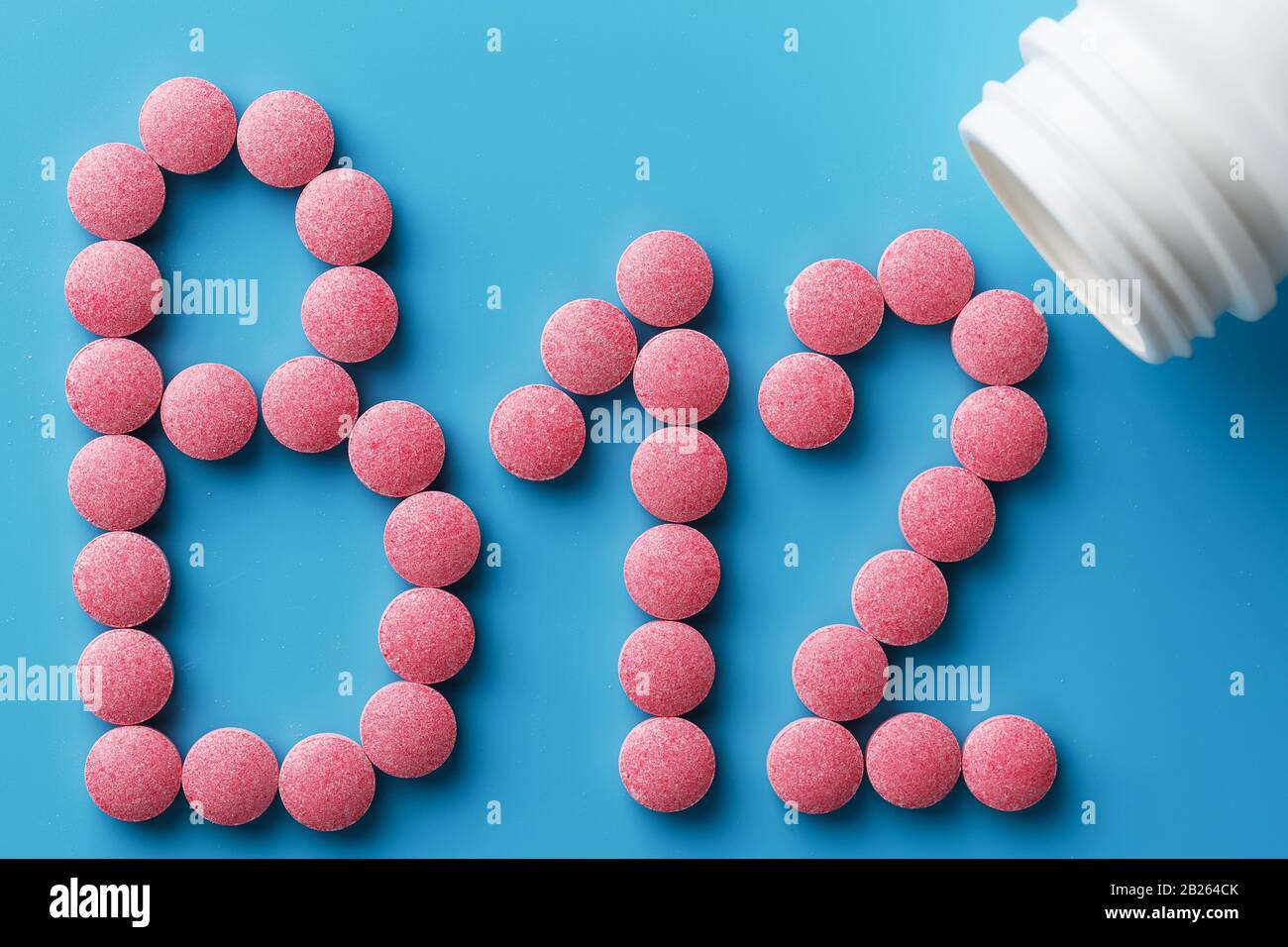 Pink pills in the shape of the letter B12 on a blue background, spilled ...