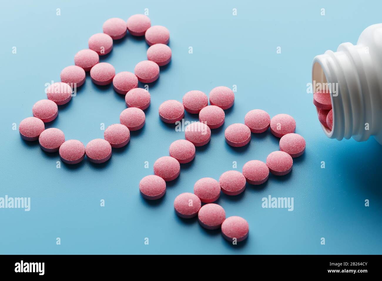 Pink pills in the shape of the letter B12 on a blue background, spilled ...