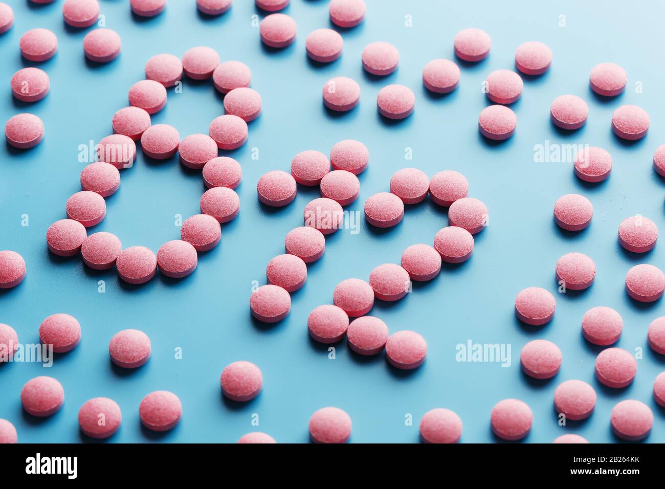 Pink pills in the shape of the letter B12 on a blue background, spilled ...