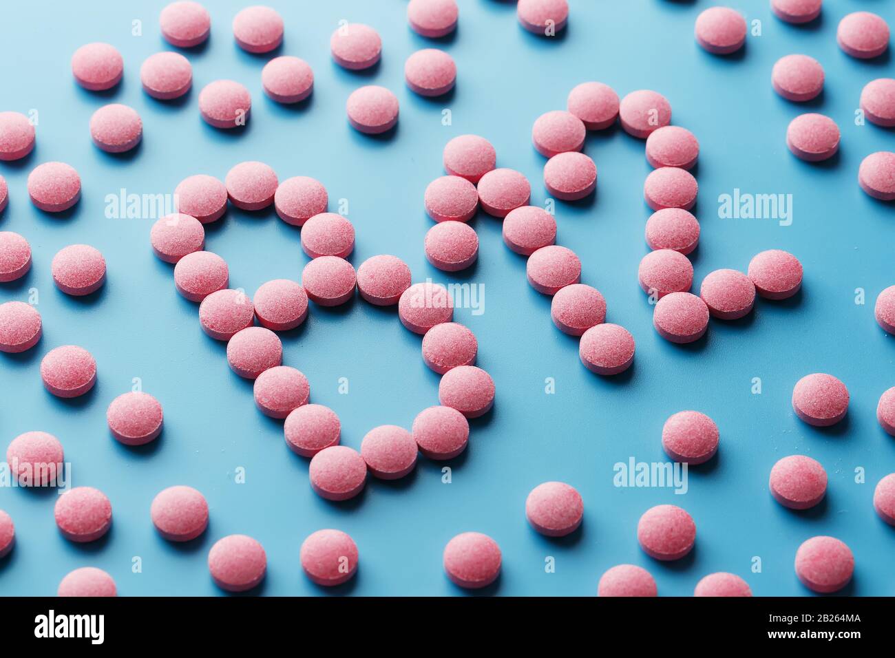 Pink pills in the shape of the letter B12 on a blue background, spilled ...