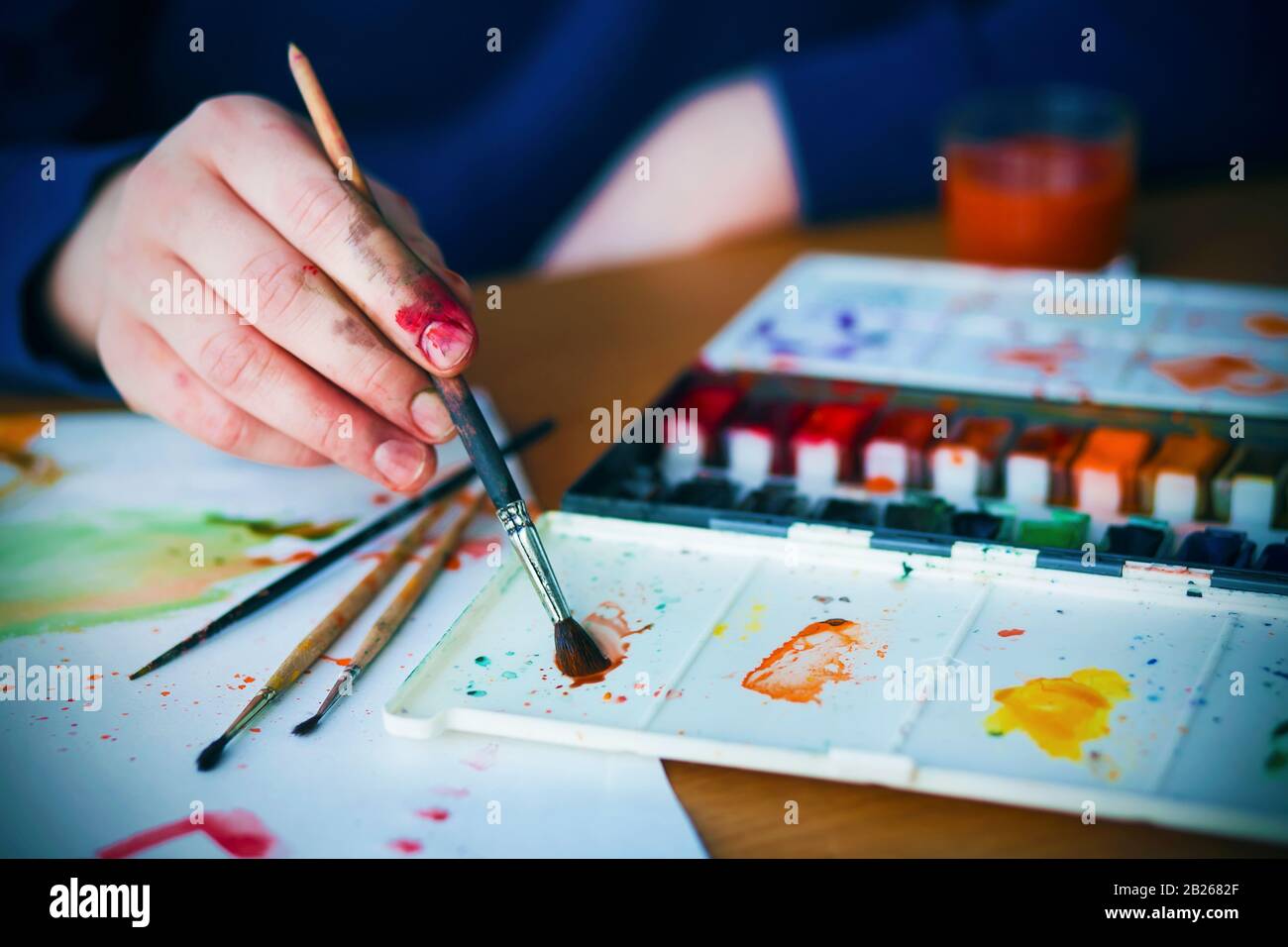 The artist's hand, with soiled fingers, gracefully holds a paintbrush ...