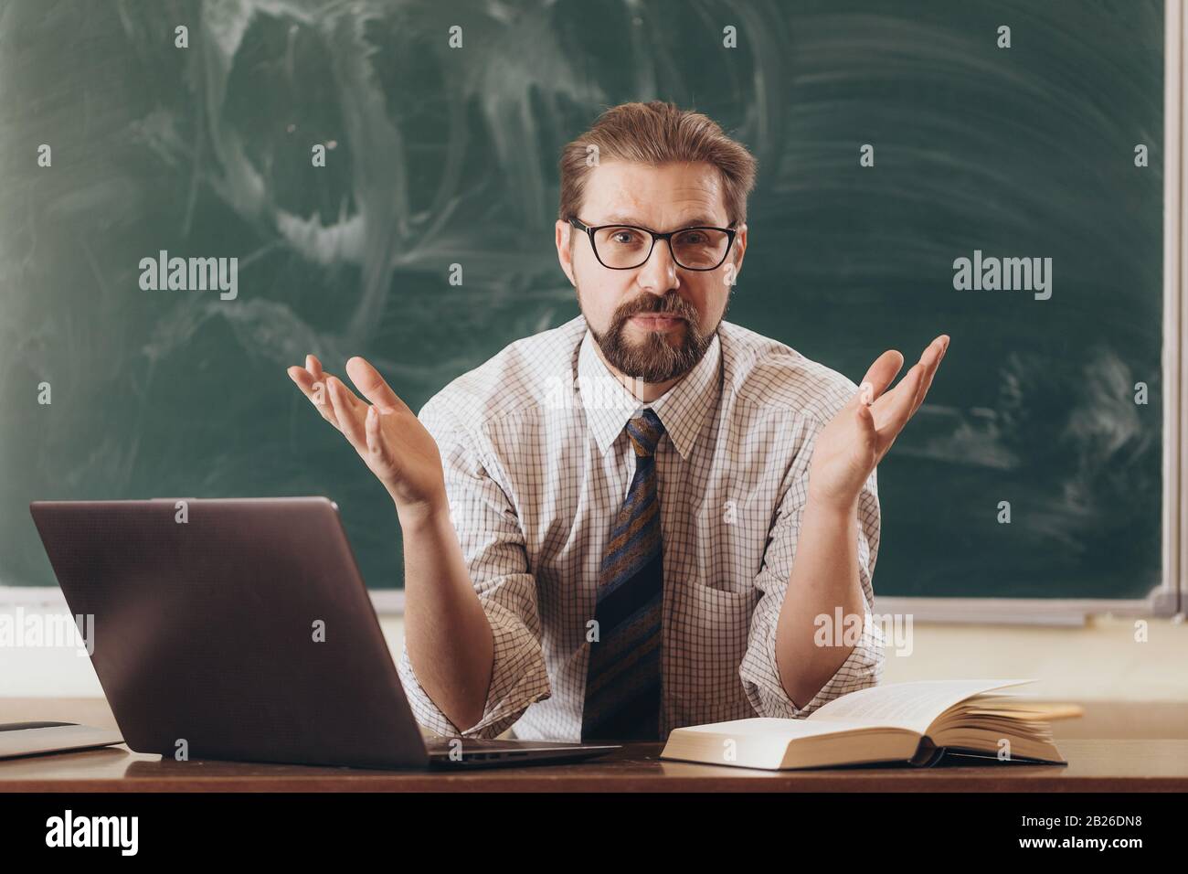 Smart bearded professor in glasses sitting by laptop at desk and ...