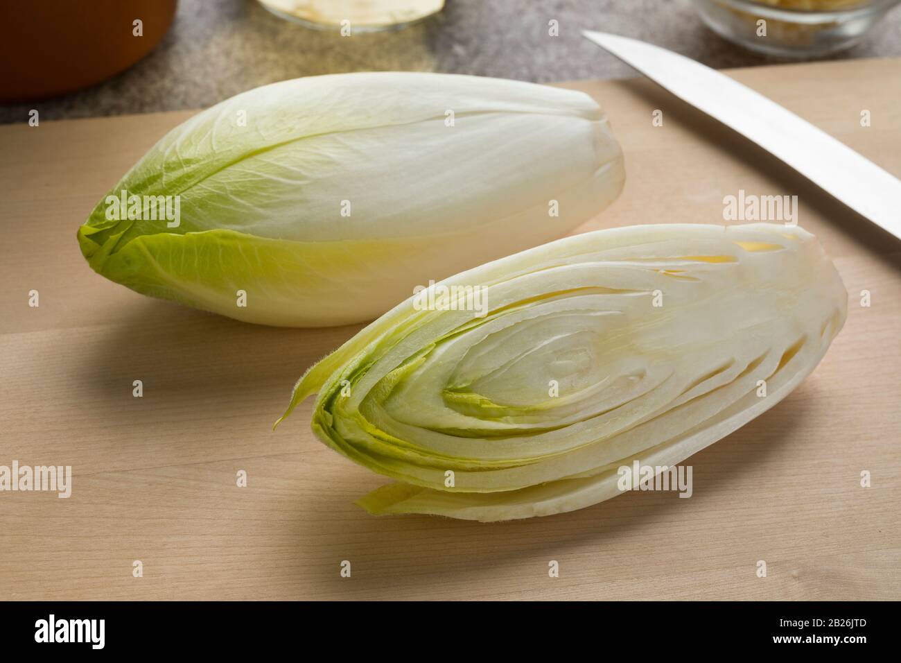 Whole and halved fresh raw Belgian endive on a cutting board Stock ...