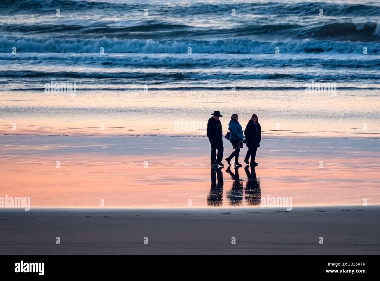 The silhouette of 3 lone people walking on the beach, with the waves ...