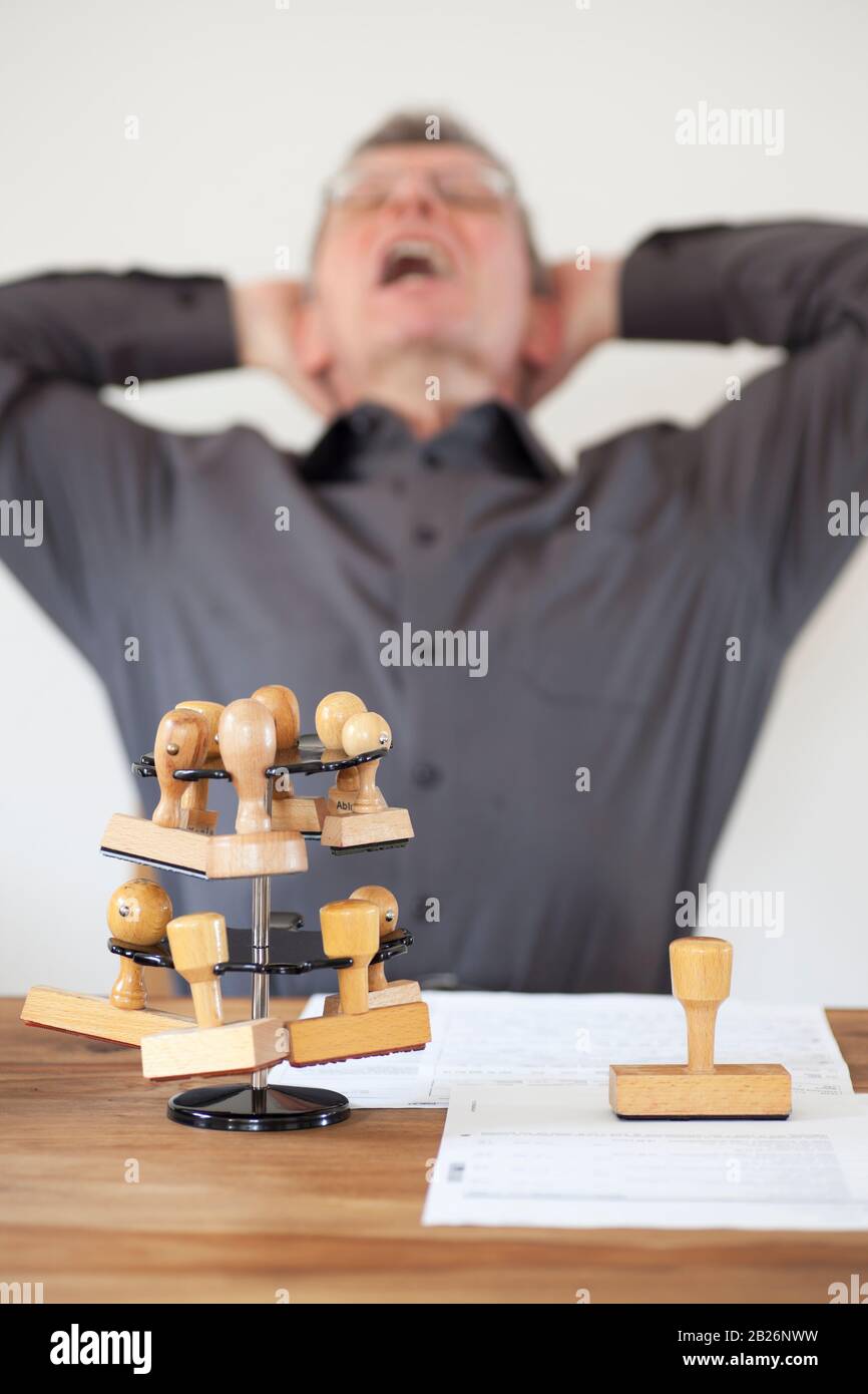 Stretching and yawning clerk at a desk with stamps and documents in an ...