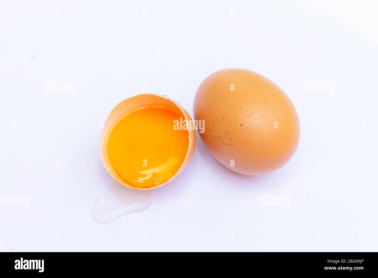 Two brown eggs With one egg broken in half, with a yolk inside the ...