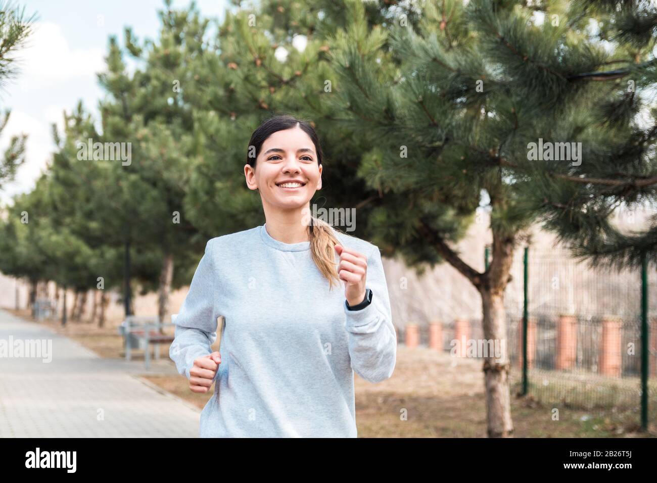healthy lifestyle. cheerful attractive woman running in park with pine ...
