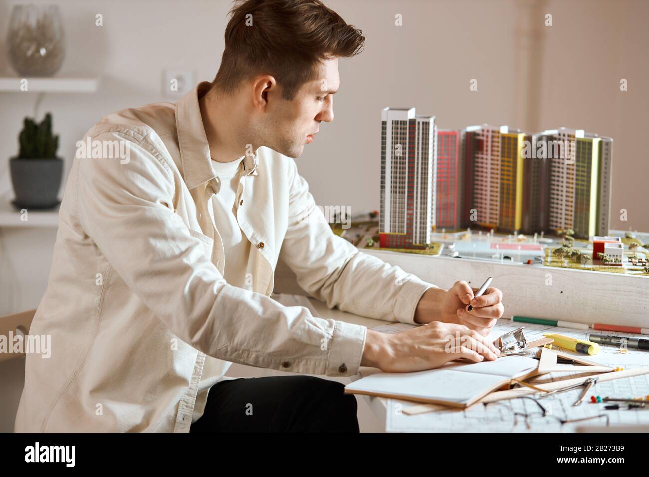 serious attractive guy drawing a new building on blueprint, looking at ...