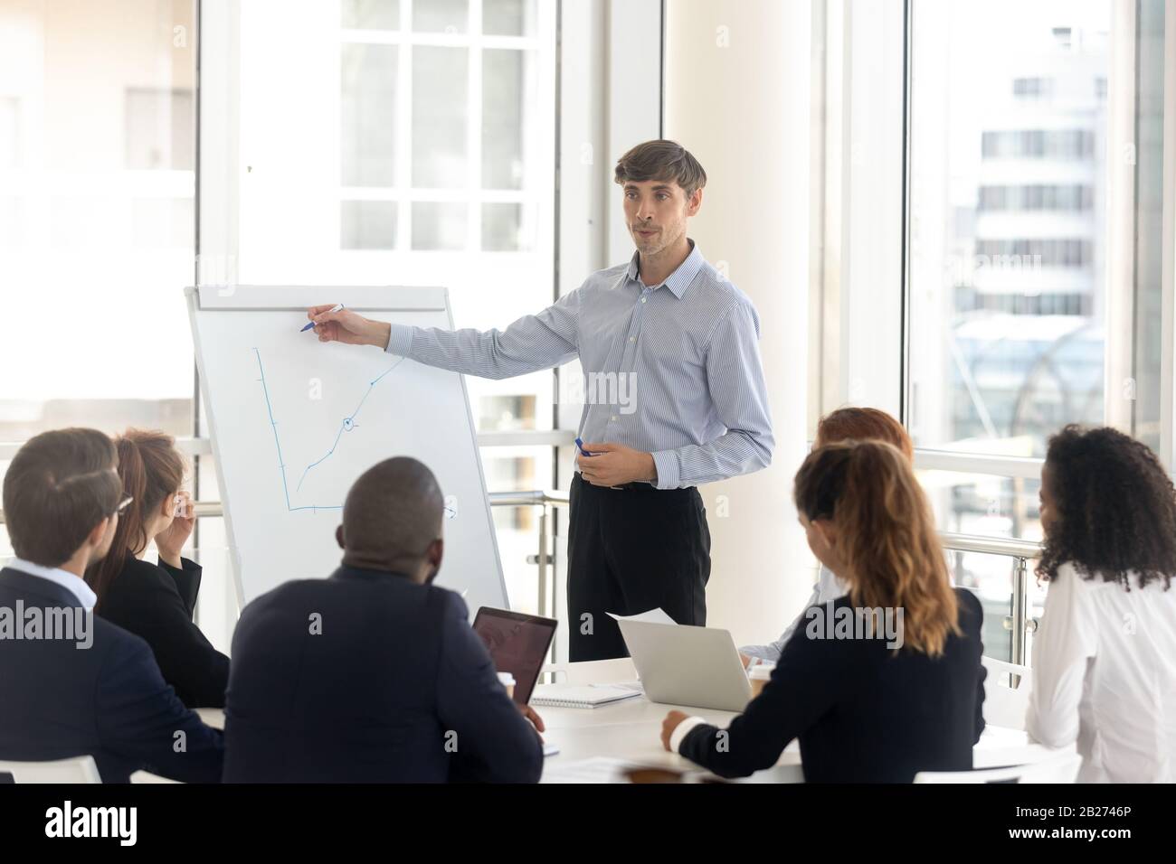 Male businessman draws graphs on flip chart at client presentation ...