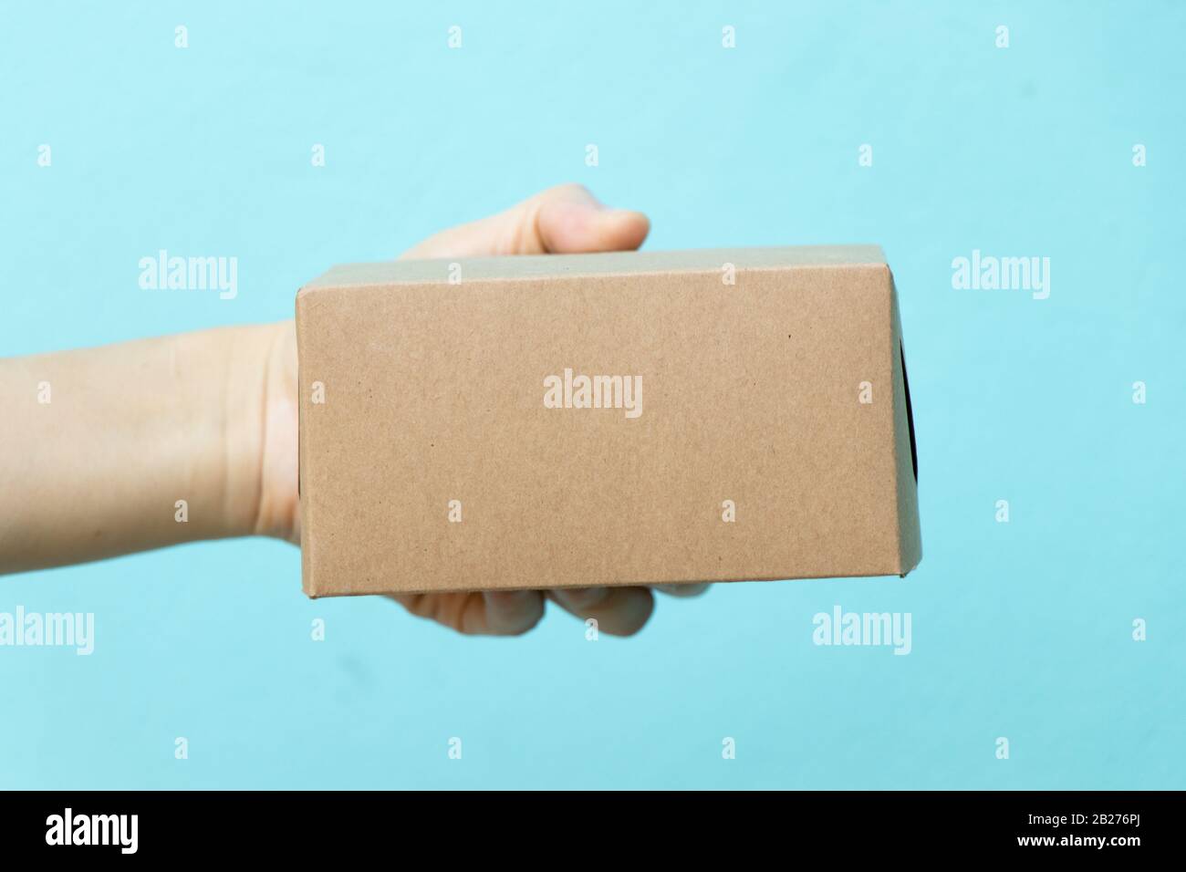 Woman hand hold the brown corrugated box on blue wall background with ...