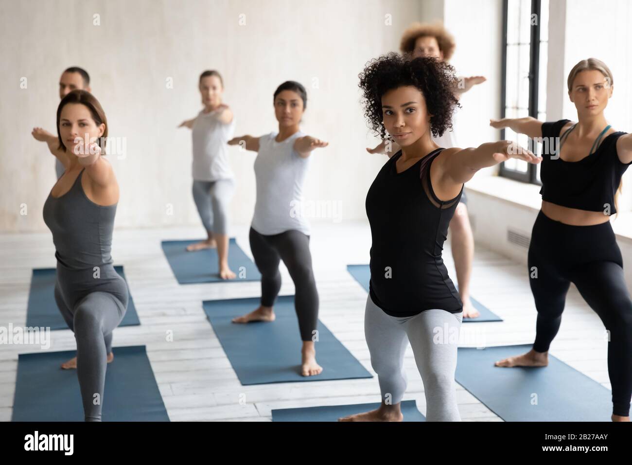 Group multiracial sporty people performing Warrior asana during yoga ...