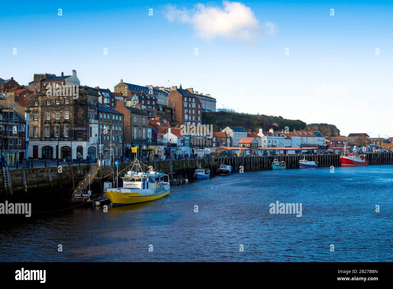 Yellow pleasure boat and blue and red fishing boats tied up at the fish ...