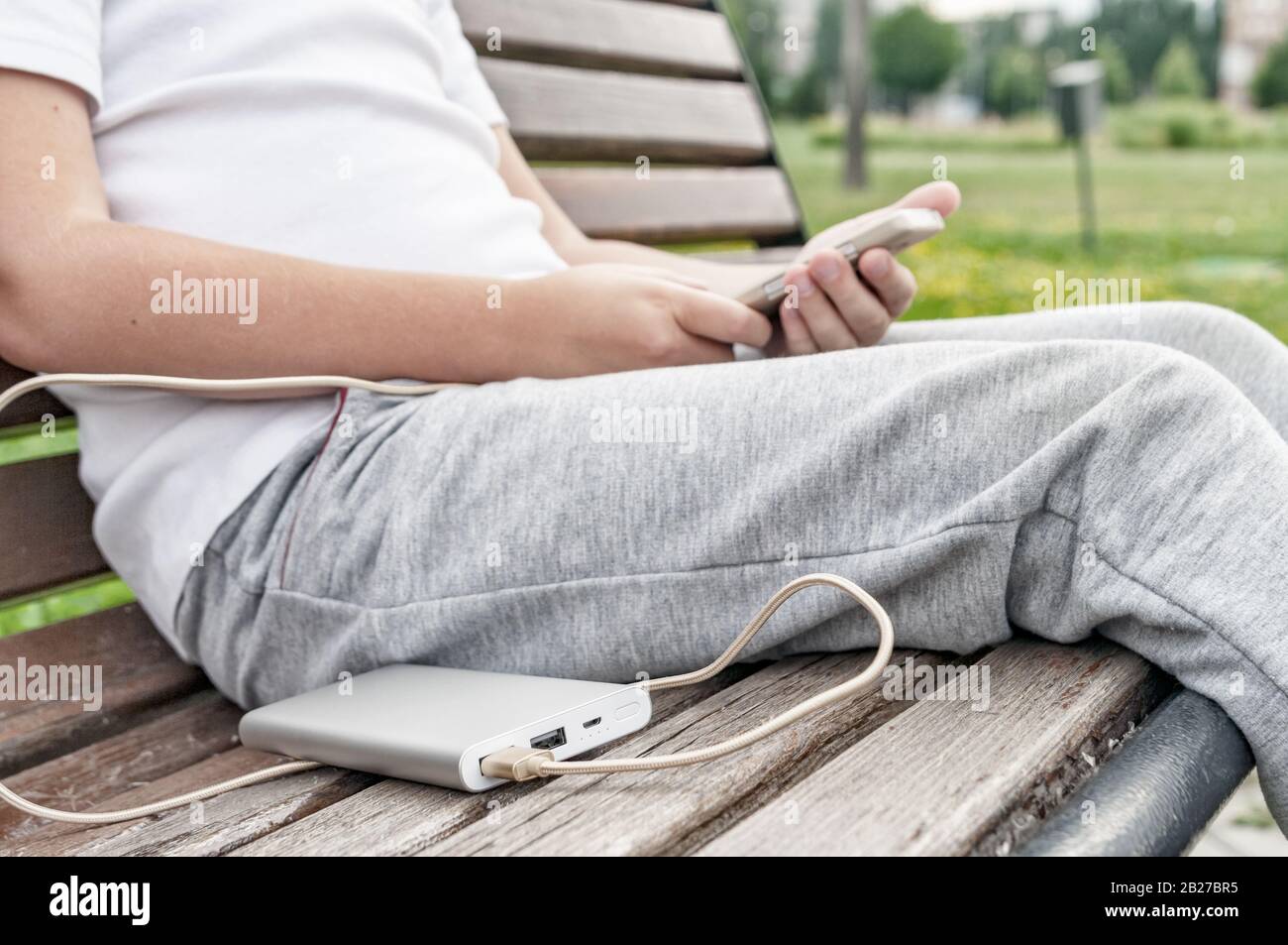 Boy using phone on the bench while charging from the power bank Stock ...