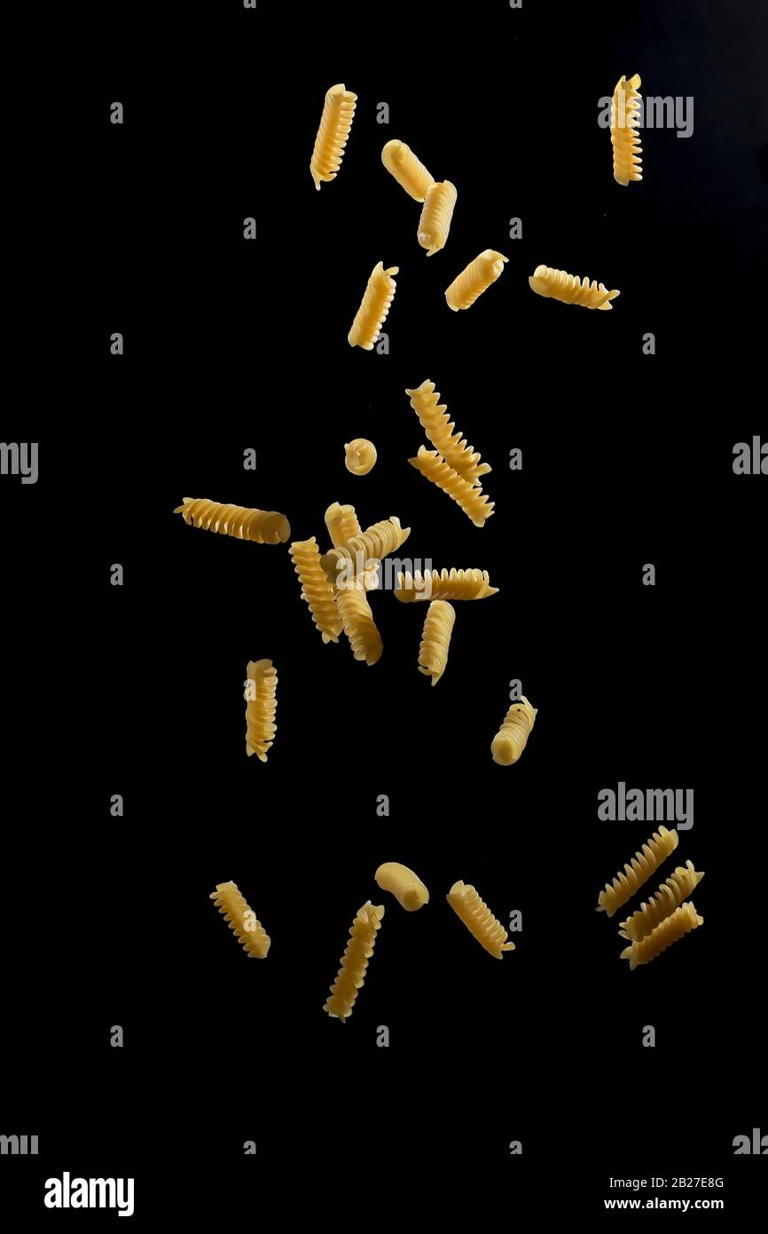 Falling fusilli pasta. Flying yellow raw macaroni over black background ...