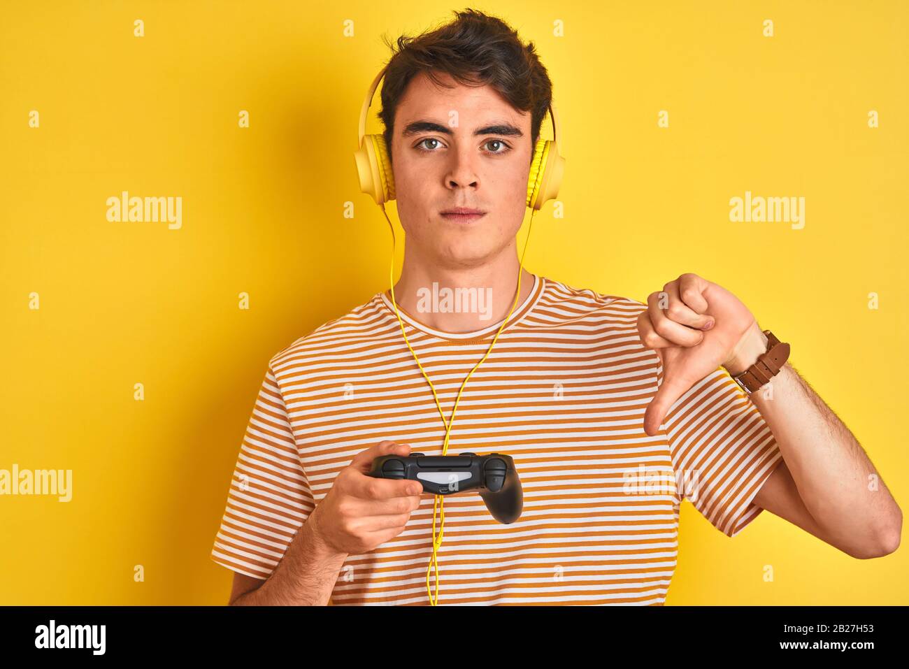 Teenager boy playing video games using gamepad over isolated yellow ...
