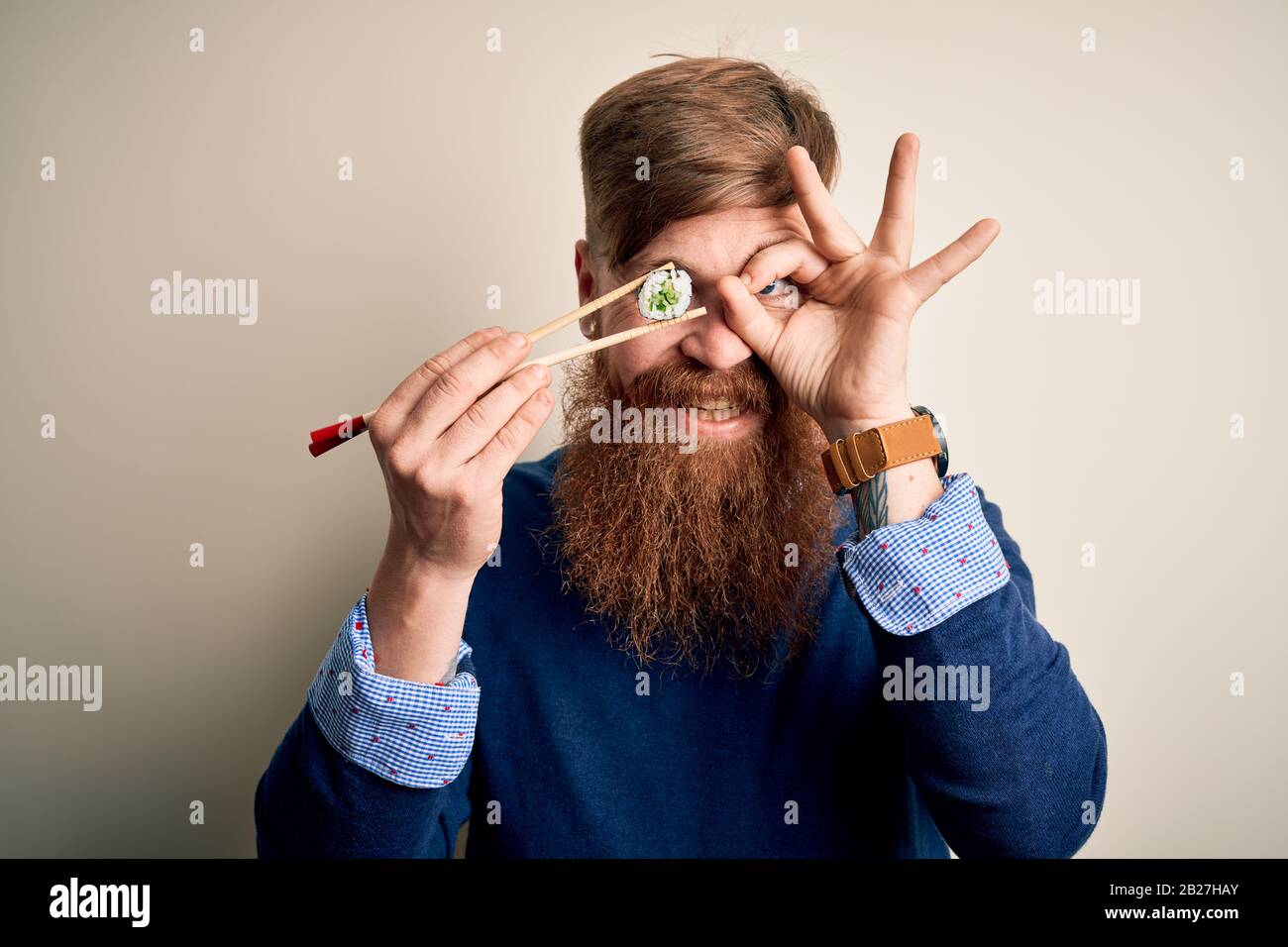 Redhead Irish Man With Beard Eating Green Maki Sushi Using Chopsticks Over Yellow Background