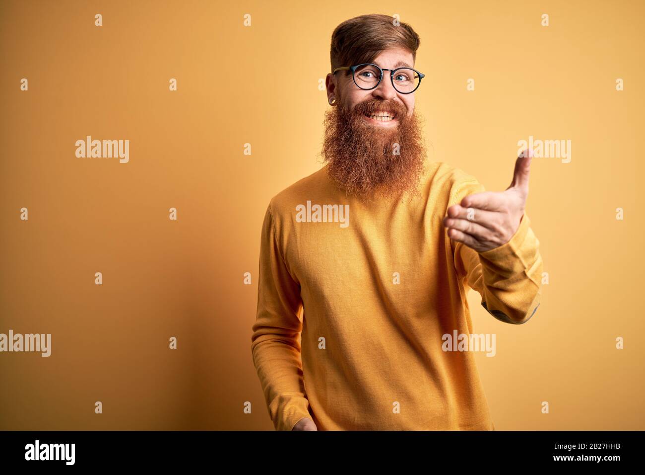 Handsome Irish redhead man with beard wearing glasses over yellow ...