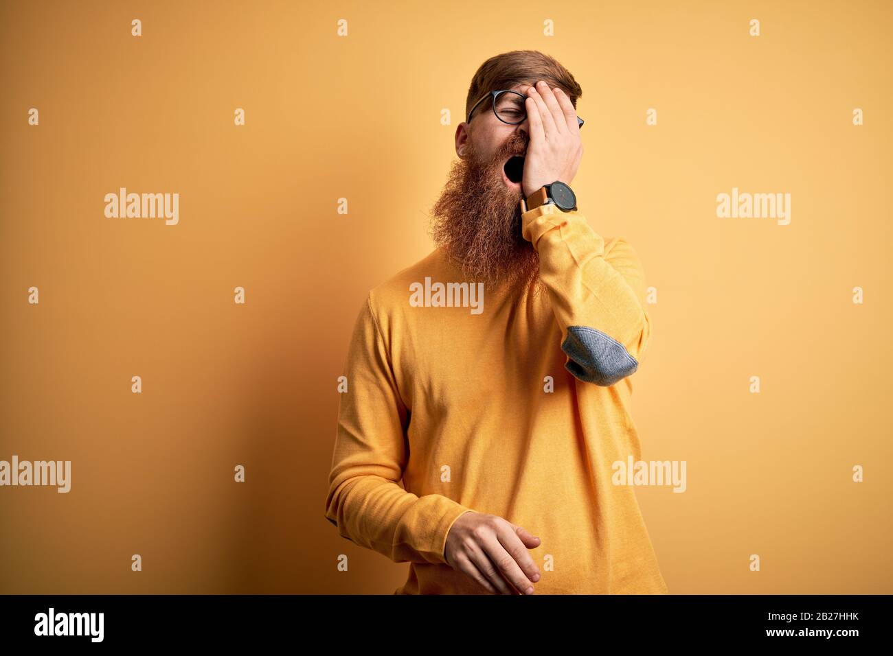 Handsome Irish redhead man with beard wearing glasses over yellow ...
