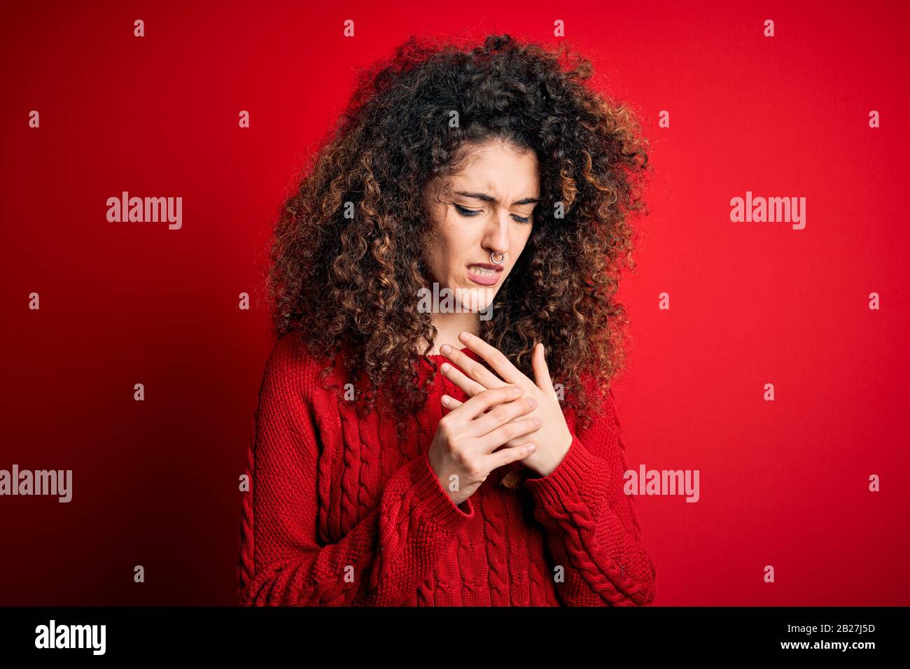 Young beautiful woman with curly hair and piercing wearing casual red ...