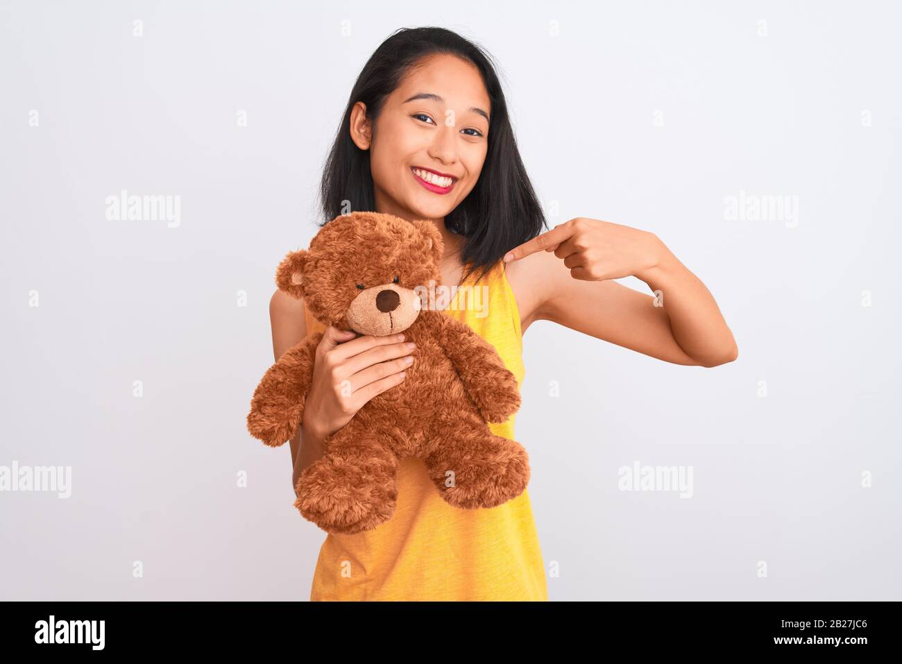 Young beautiful chinese woman holding teddy bear standing over isolated ...