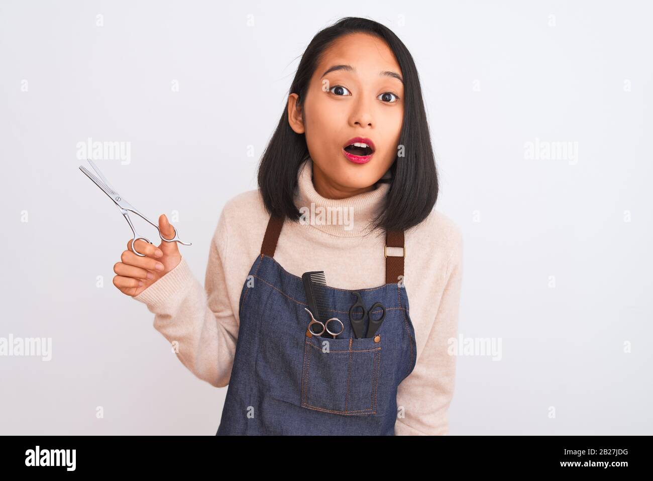 Chinese hairdresser woman wearing apron holding scissors over isolated white background scared ...